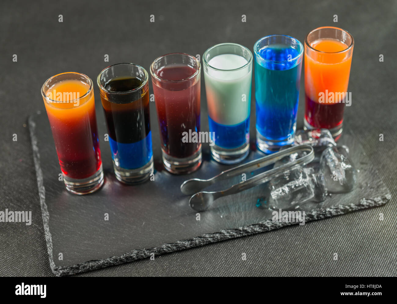 left side view on a six different colored shot drinks, lined up on a ...