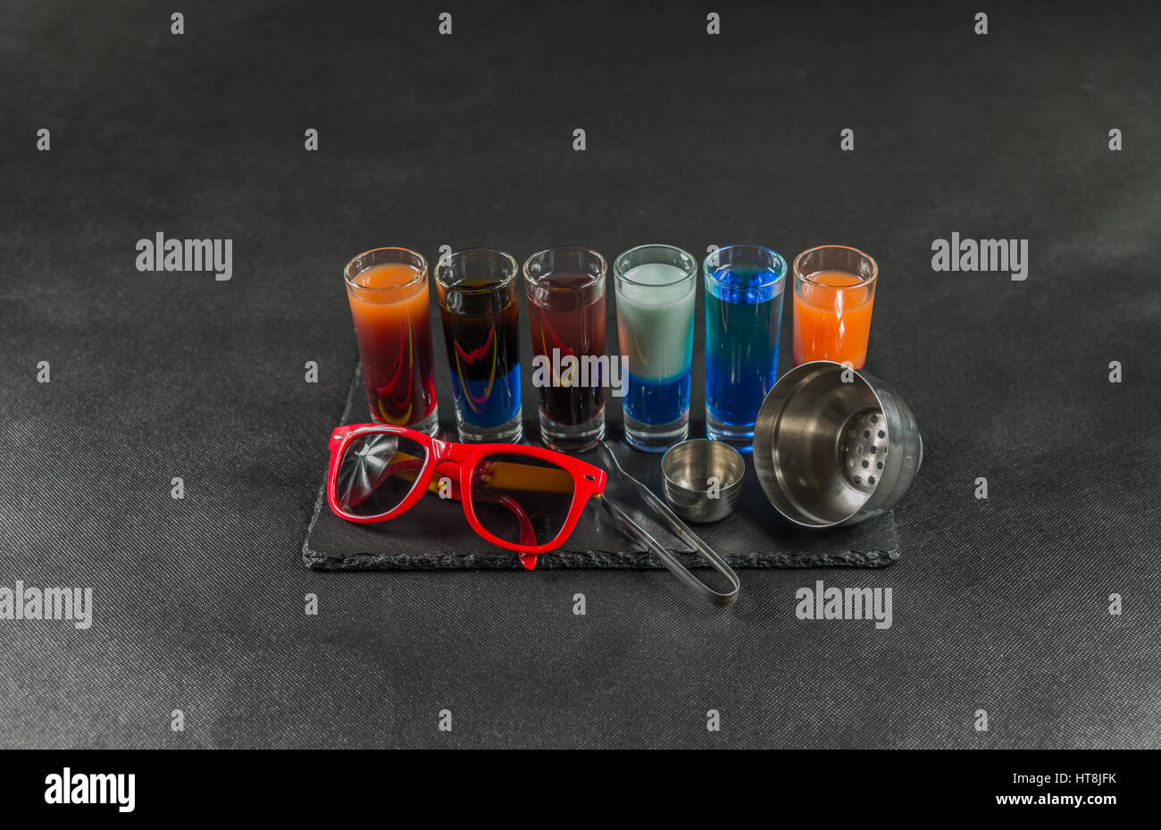 six different colored shot drinks, lined up on a black stone plate, ice ...