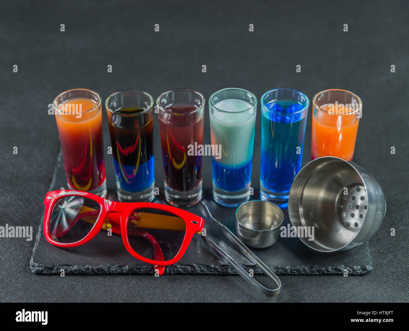 six different colored shot drinks, lined up on a black stone plate, ice ...