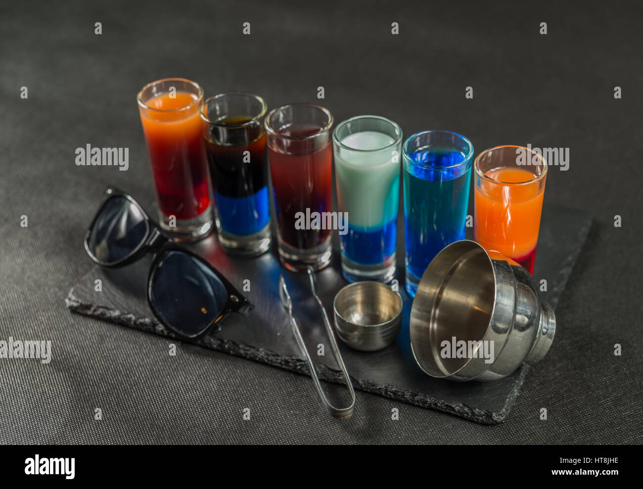 six different colored shot drinks, lined up on a black stone plate, ice ...