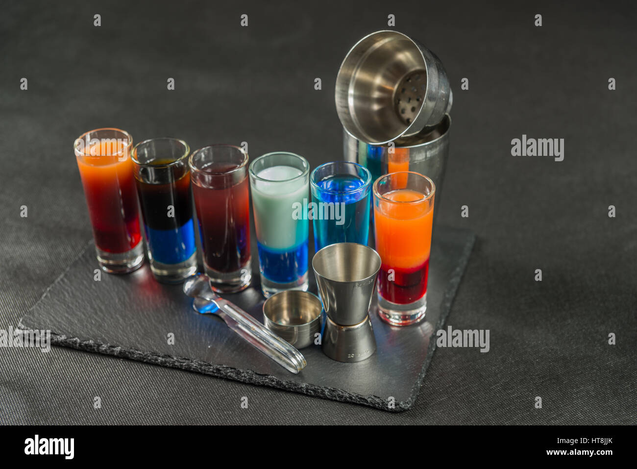 six different colored shot drinks, lined up on a black stone plate, ice ...