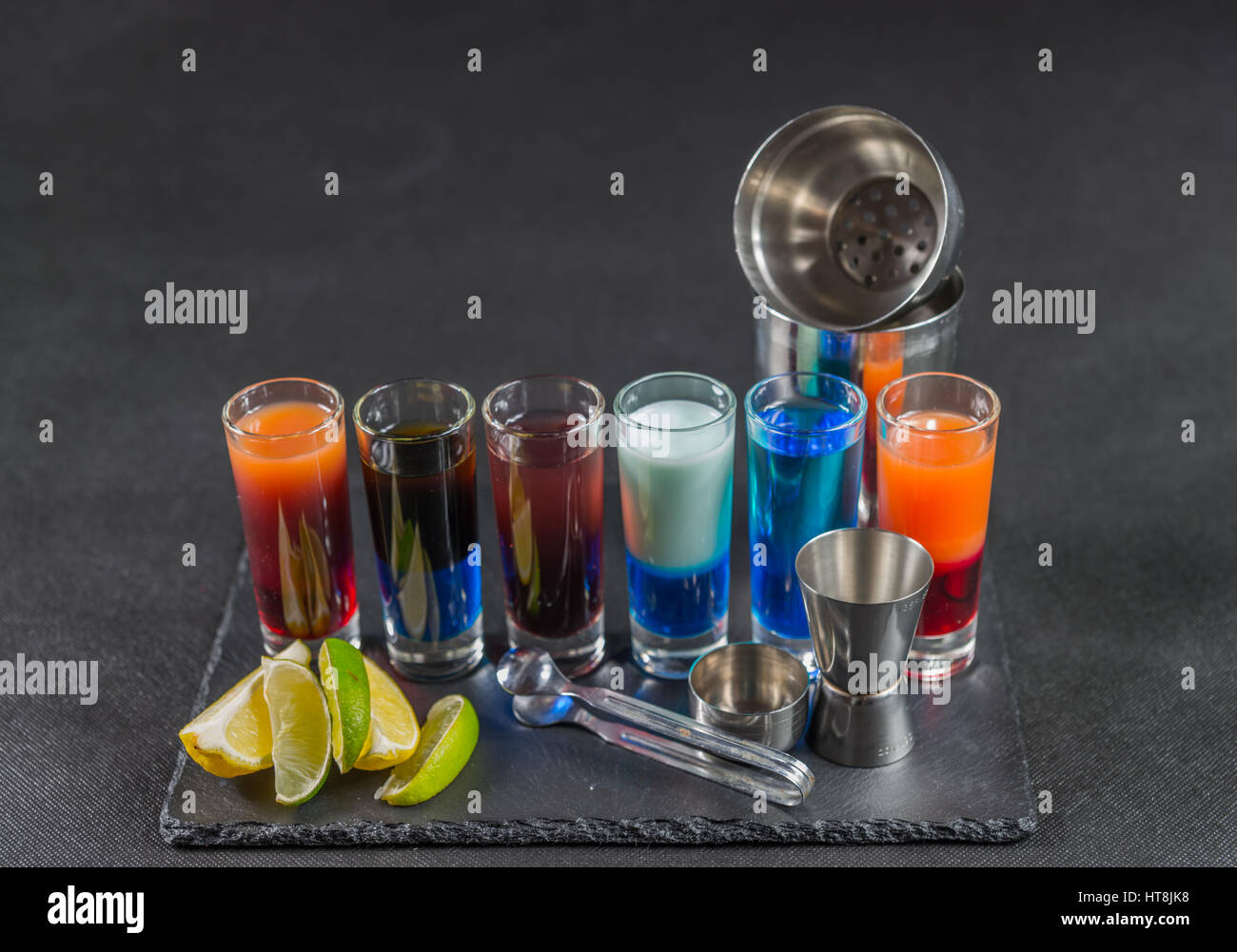 six different colored shot drinks, lined up on a black stone plate, ice ...