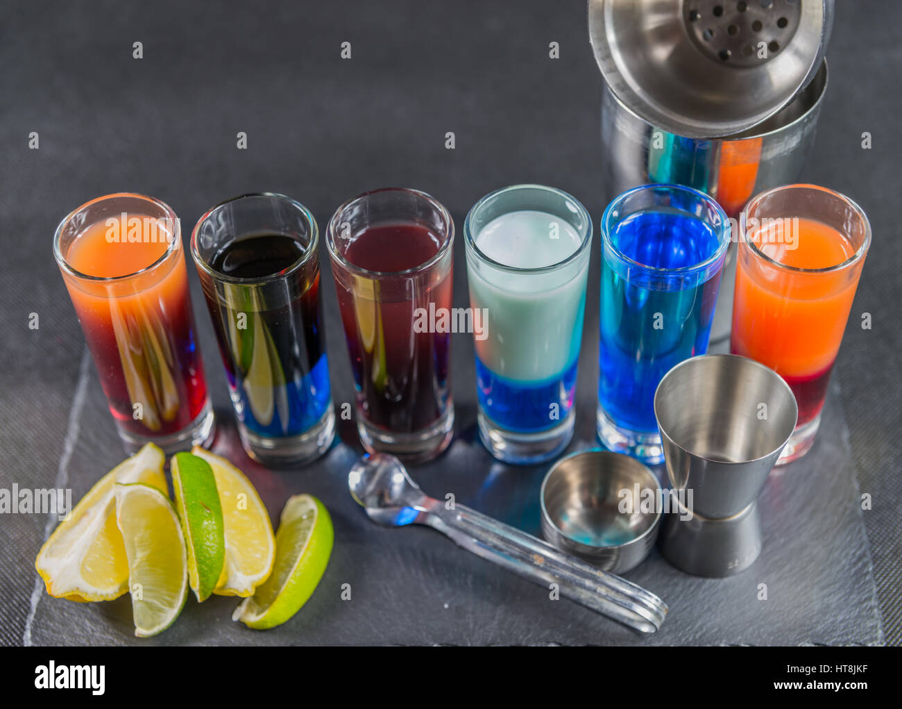 six different colored shot drinks, lined up on a black stone plate, ice ...