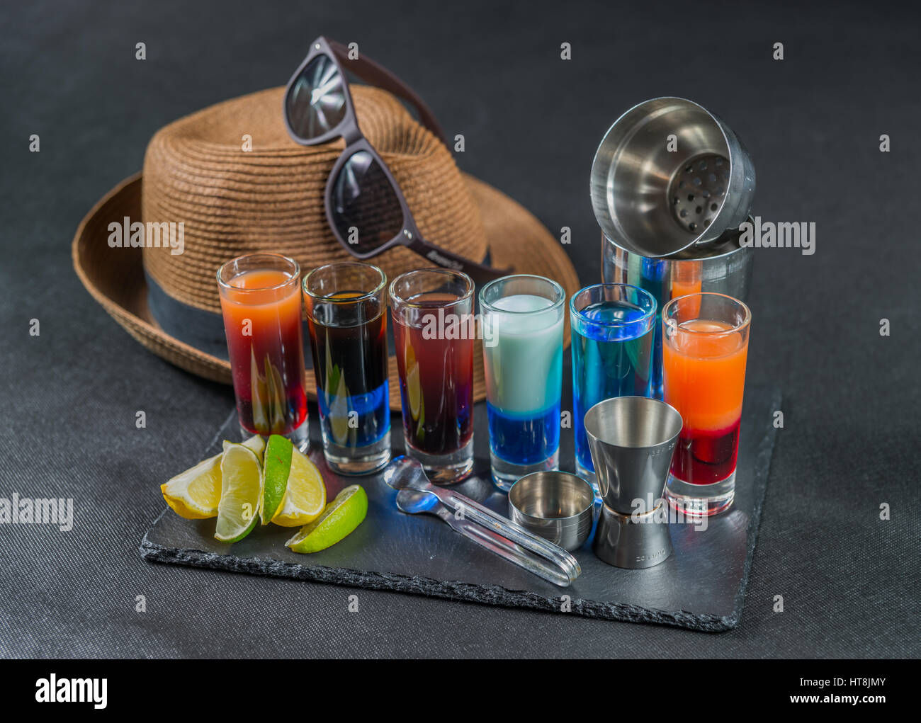 six different colored shot drinks, lined up on a black stone plate, ice ...
