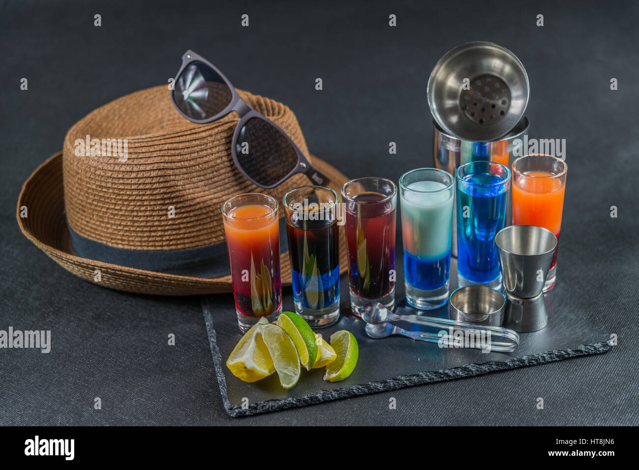 six different colored shot drinks, lined up on a black stone plate, ice ...