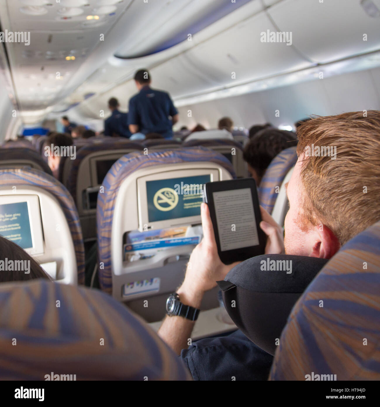 Rear view of airplane cabin with unrecognizable male passenger reading ...