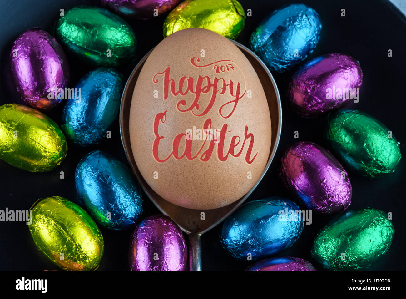 Happy Easter 2017 lettering written on Easter Egg placed on silver spoon with small chocolate ...