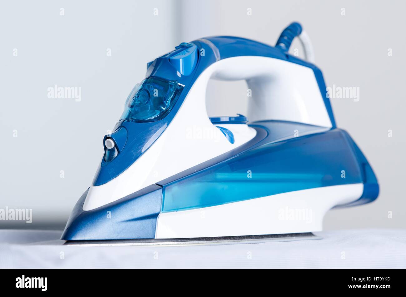 Modern blue steam iron on ironing board close up Stock Photo - Alamy