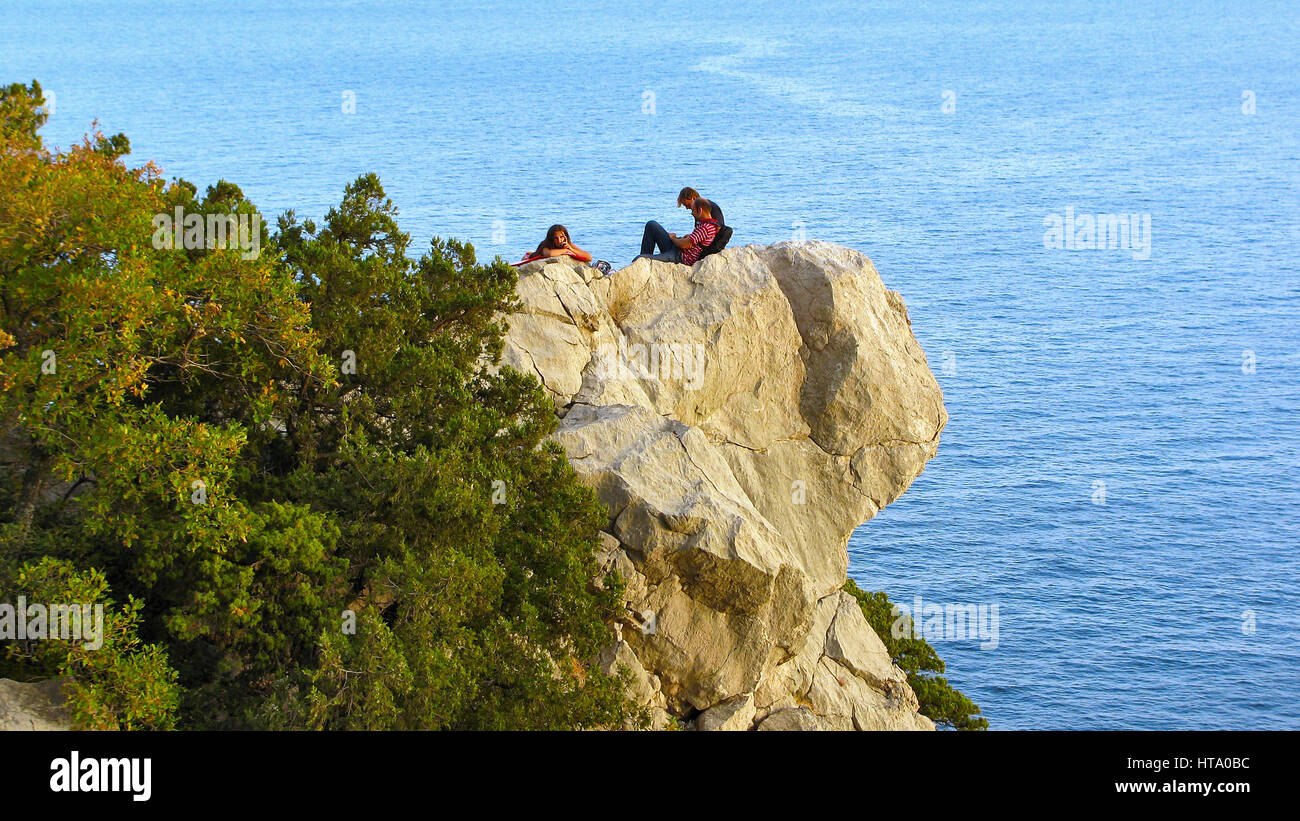 Two men and a woman resting on a ledge of rock above the sea Stock ...