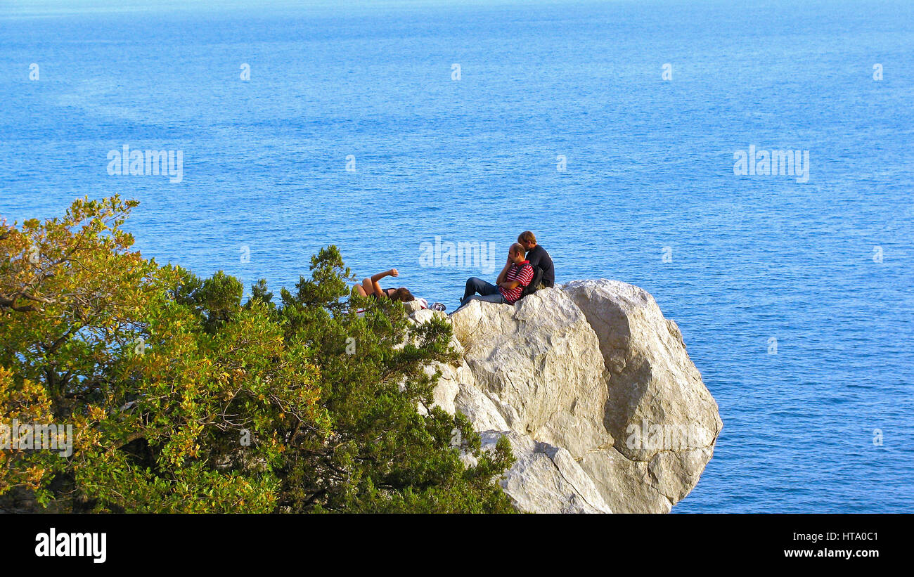 A group of people settled down to rest on a rock above the sea Stock ...