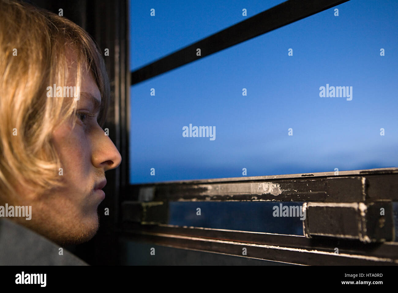 Young man looking through window Stock Photo - Alamy