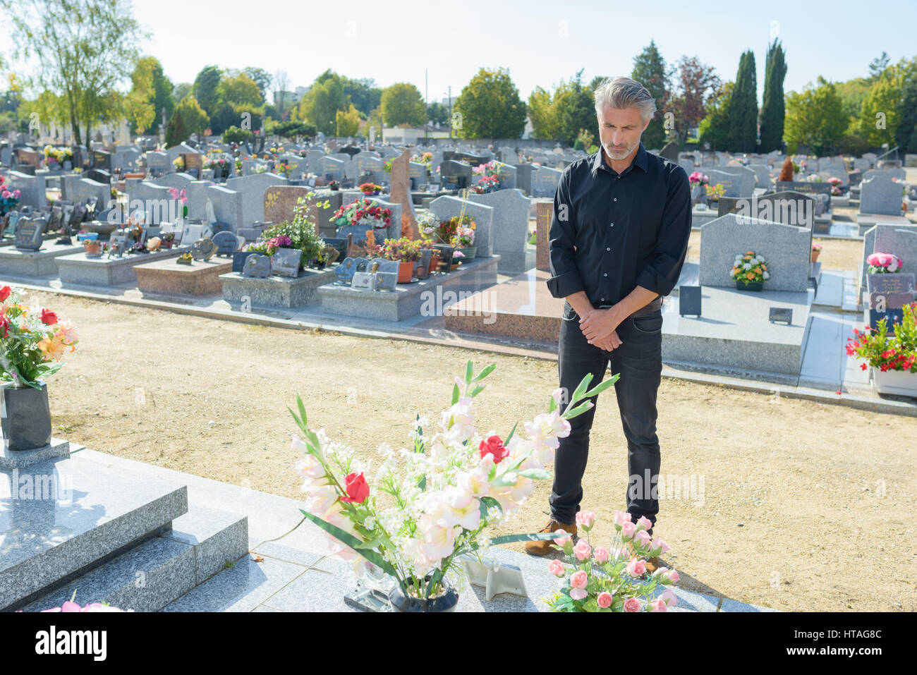 Man stood looking at gravestone Stock Photo - Alamy