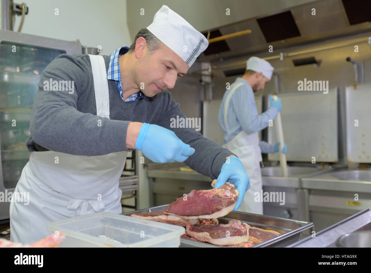 apprentice and chief preparing meat in restaurant kitchen Stock Photo ...