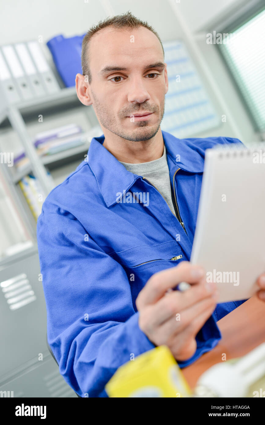 Man in overalls looking at notepad Stock Photo - Alamy