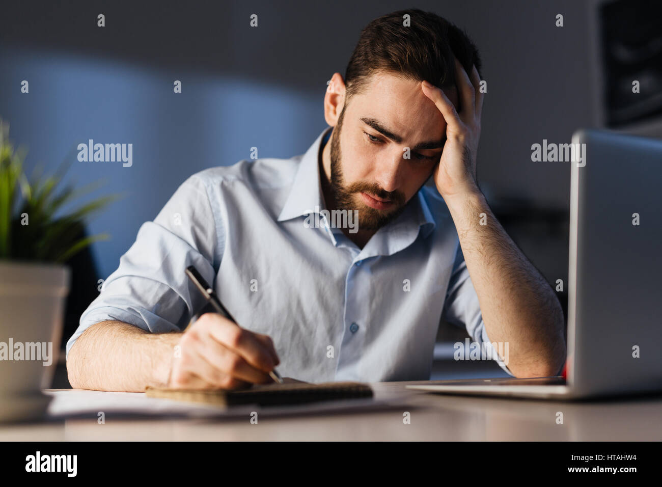 Tired man writing plan of work in office in late evening Stock Photo ...