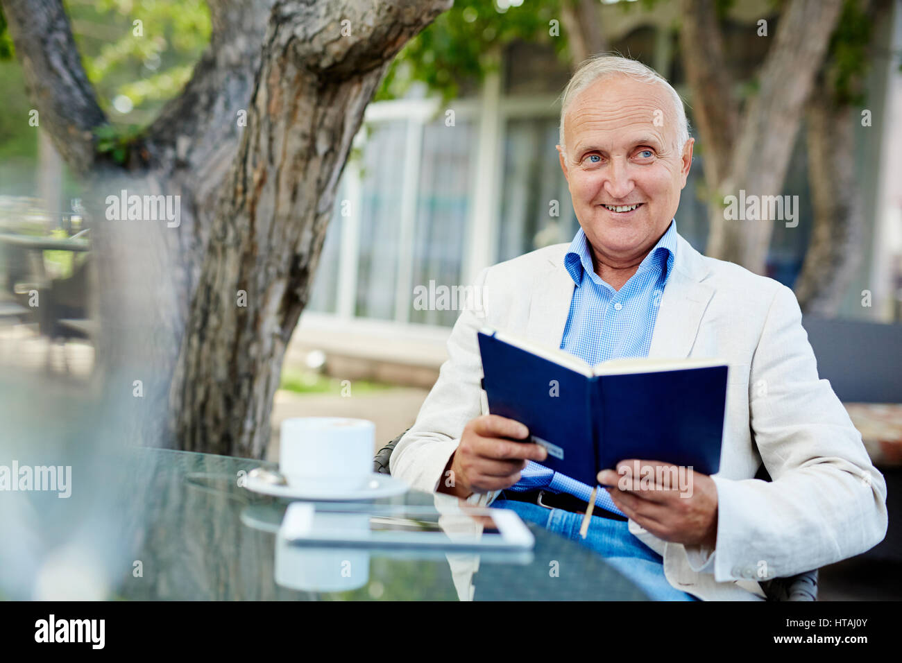 Nice elegant old man smiling kindly looking up from reading a book in ...