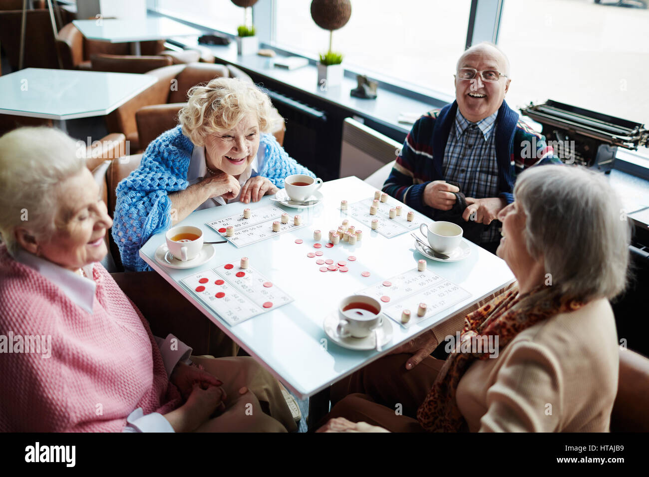 Group of elderly people sitting by table, talking and playing lotto ...