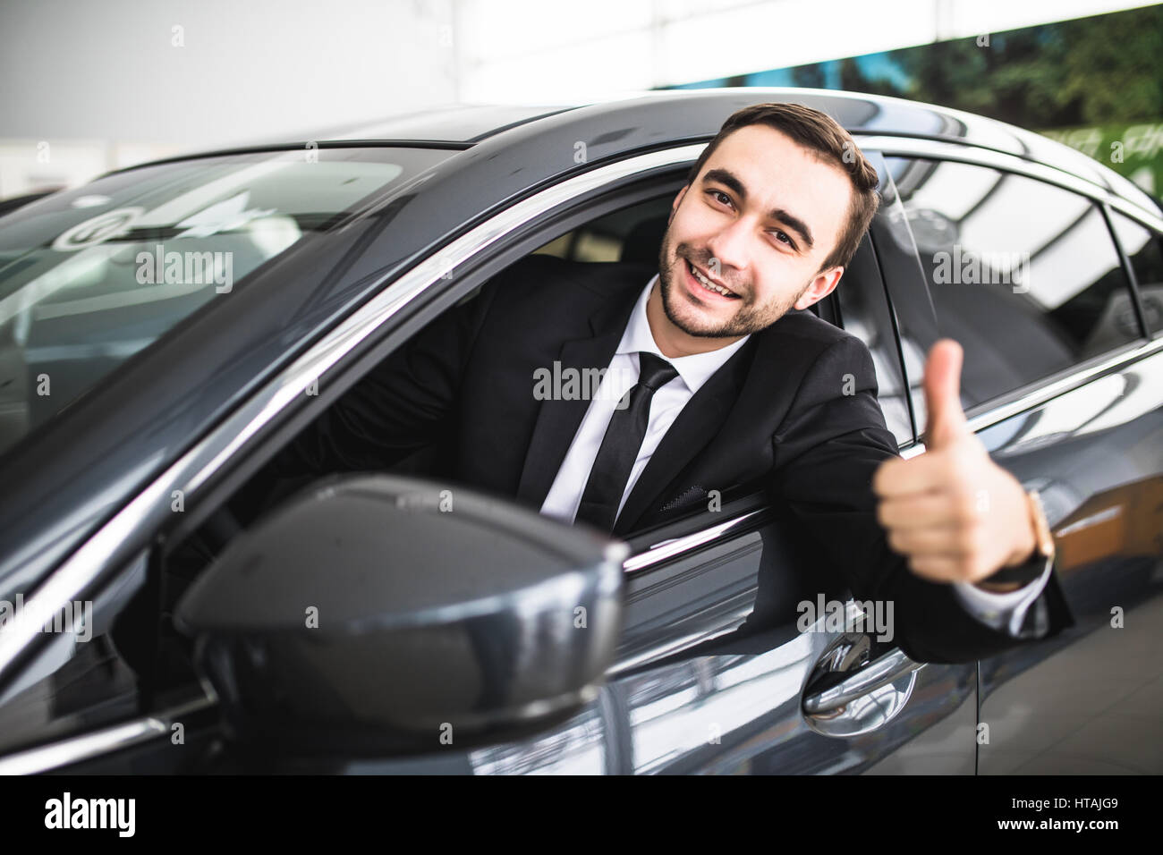 Businessman smiling at camera showing thumbs up in his car over window ...