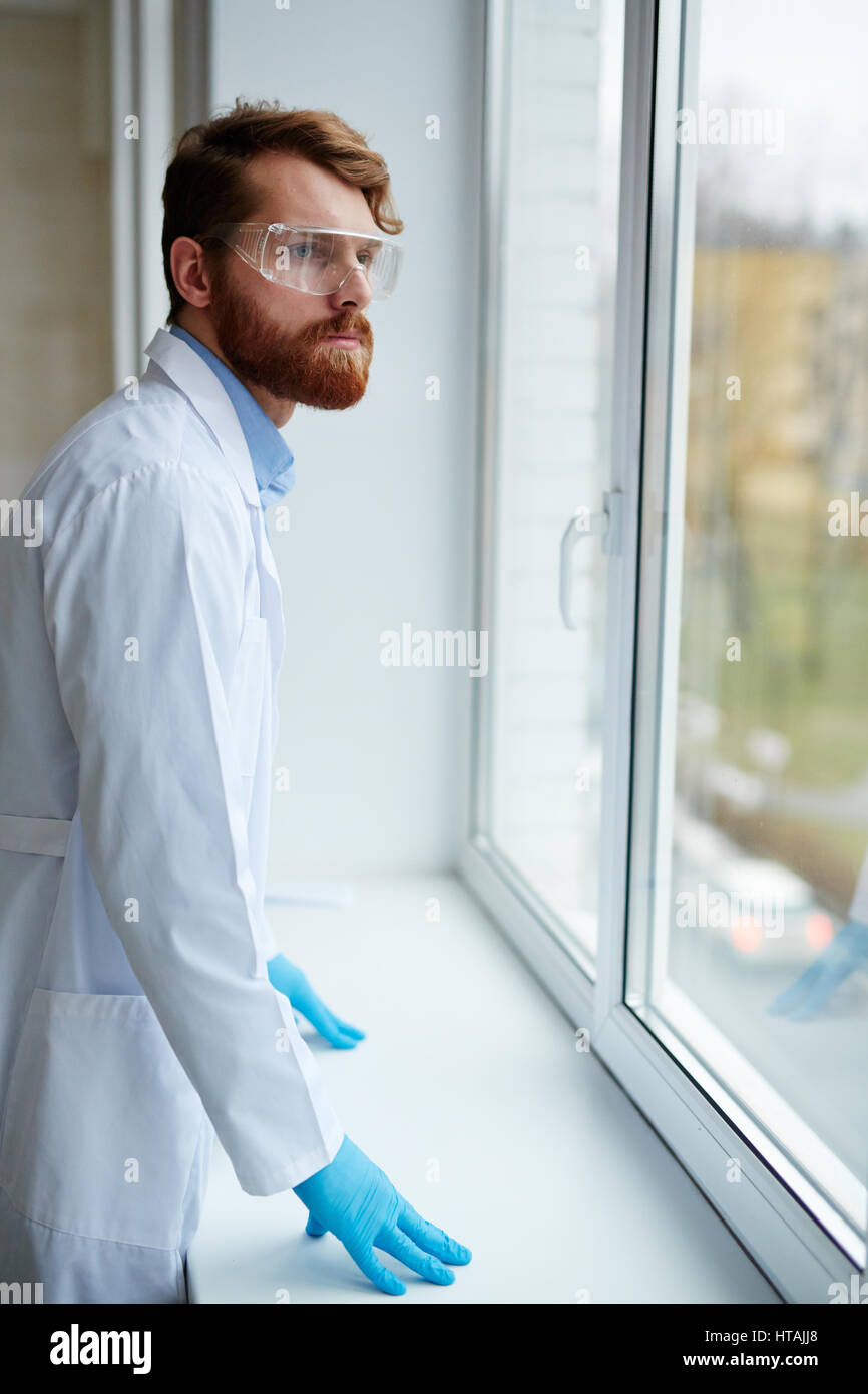 Serious young man in uniform looking through lab window Stock Photo - Alamy