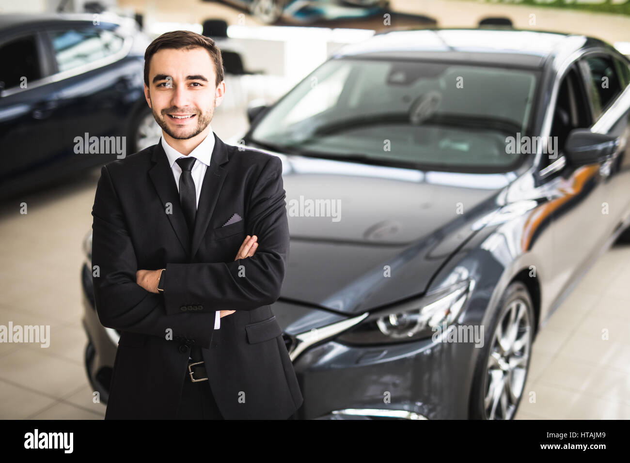 Handsome young classic car salesman standing at the dealership in front ...