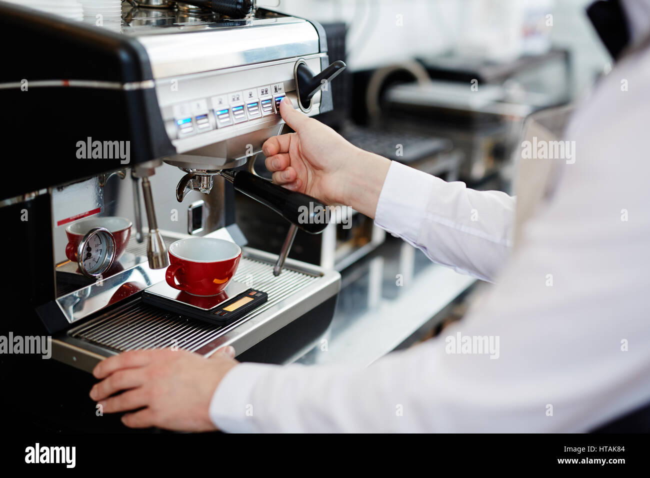 Barista pressing button on coffee-machine to start pouring espresso ...