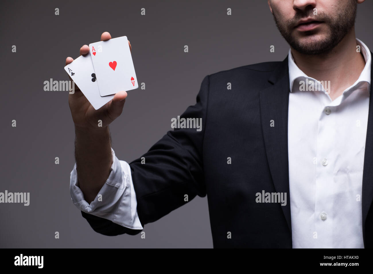 Closeup of man magician with two playing cards in his hand over grey ...