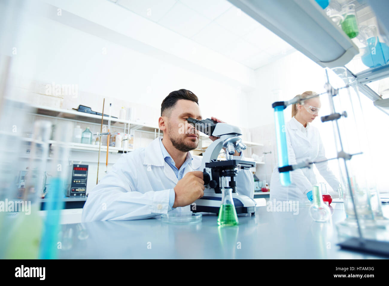 Laboratory worker sitting by table with microscope Stock Photo - Alamy
