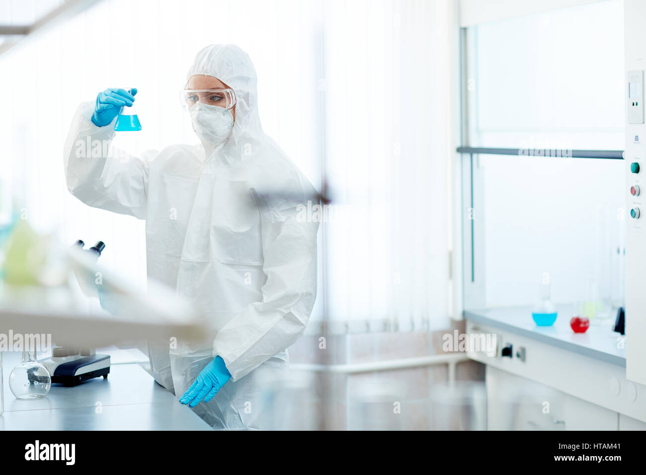 Pharmacologist in protective overalls looking at dangerous toxic fluid ...