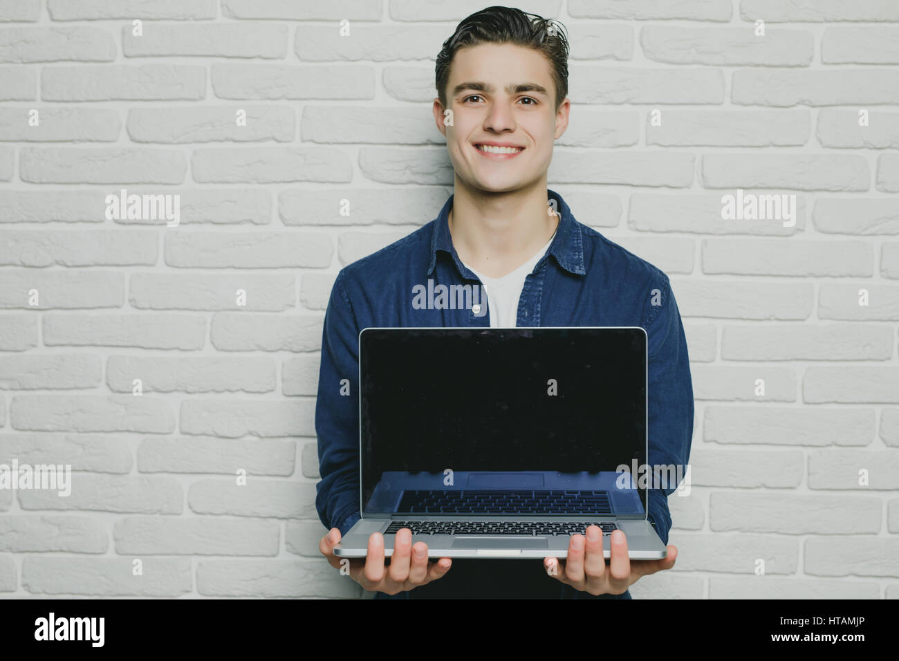 Young handsome man point the finger at a blank screen laptop, looking ...