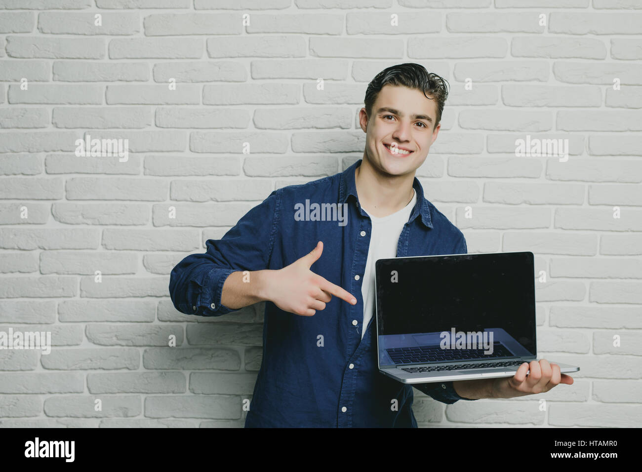 Young handsome man point the finger at a blank screen laptop, looking ...