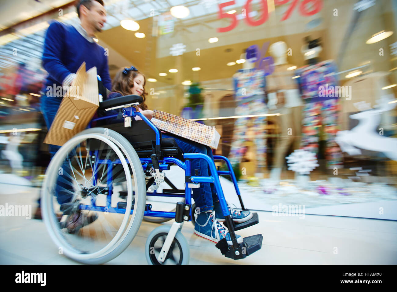 Man pushing wheelchair with daughter in shopping-center Stock Photo - Alamy