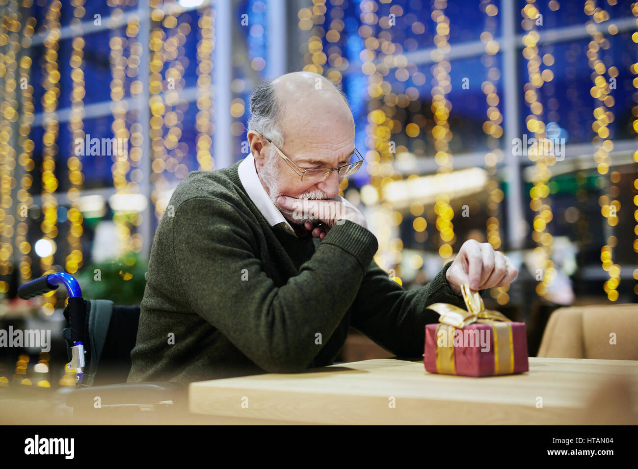 Disabled senior man looking at gift-box on table Stock Photo - Alamy