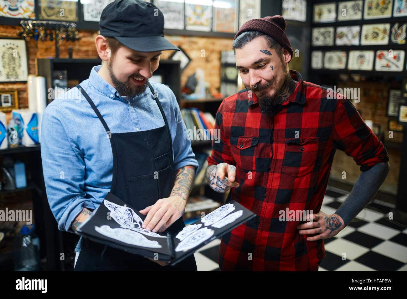 Master of tattoo helping his client to choose ornament Stock Photo - Alamy