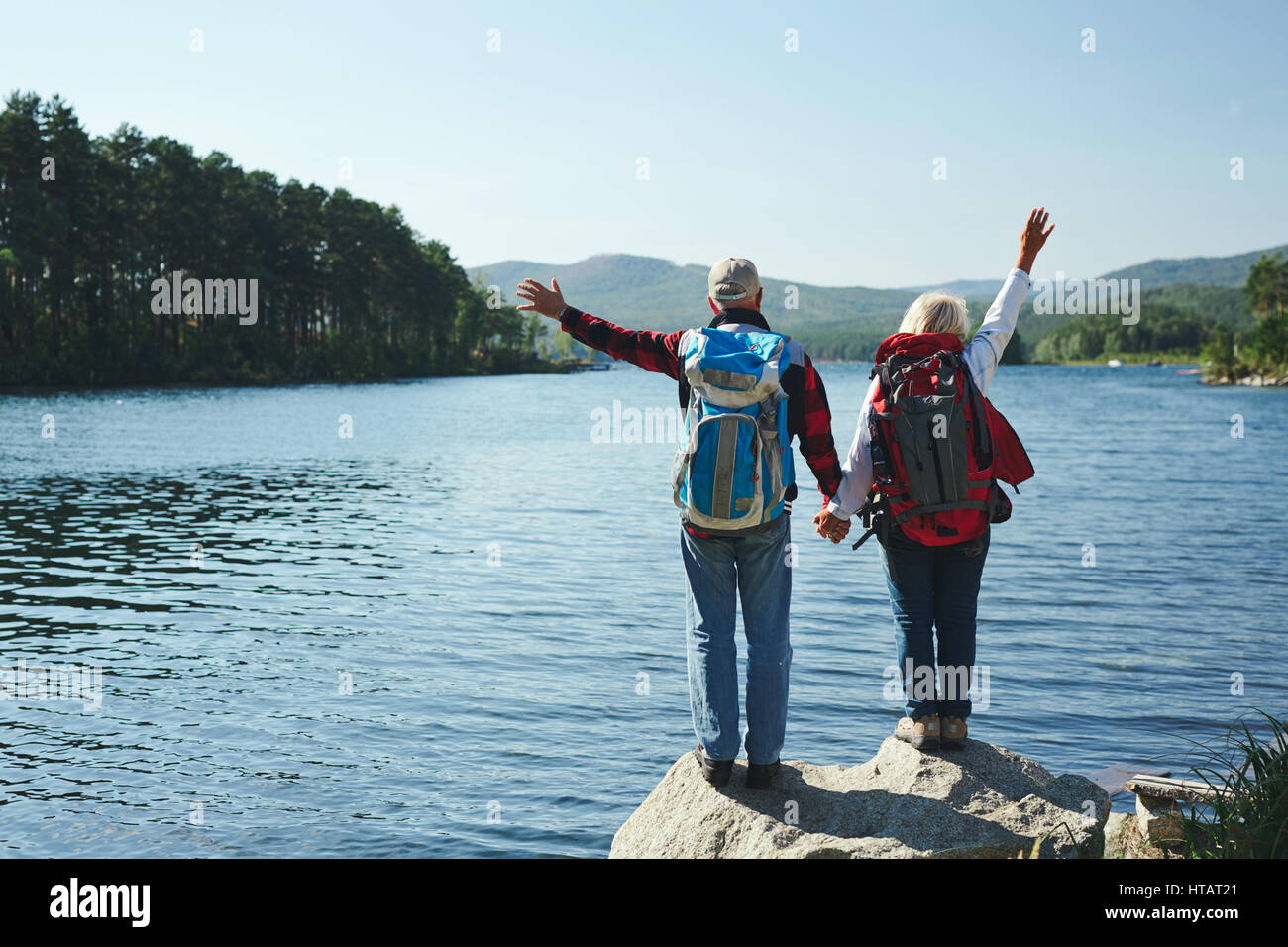 Adventurous seniors waving hands in front of lake Stock Photo - Alamy