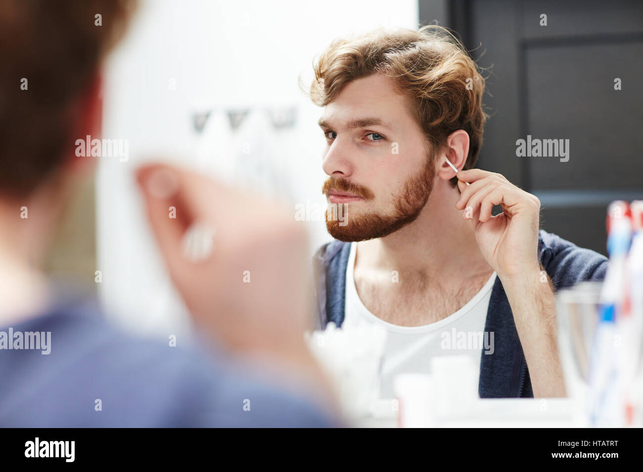 Young man cleaning his ears in front of mirror Stock Photo - Alamy