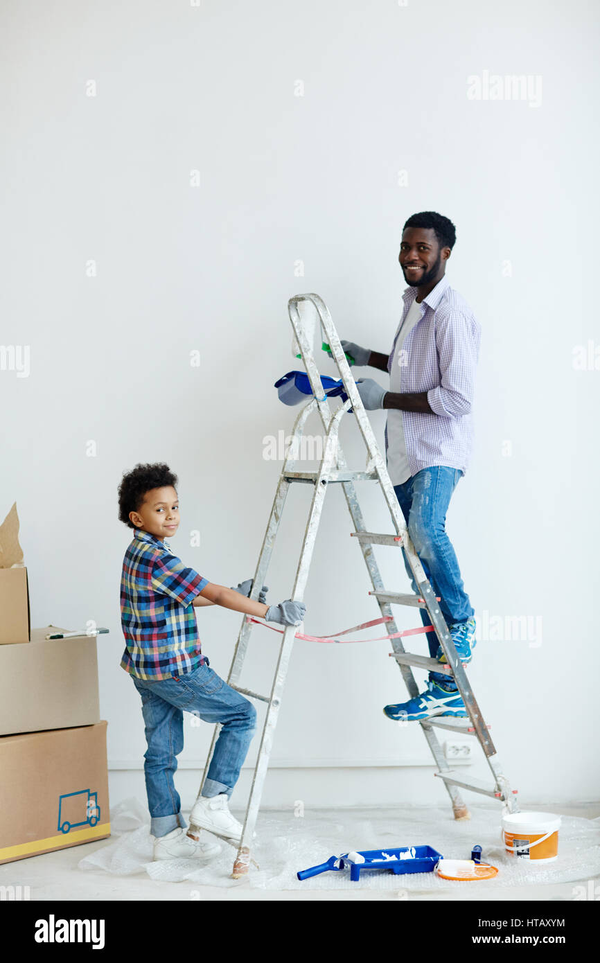 Boy holding ladder while his father painting wall in new flat Stock ...