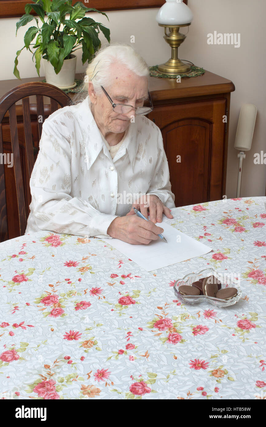 The old woman signs documents sitting at the table.The old woman writes ...