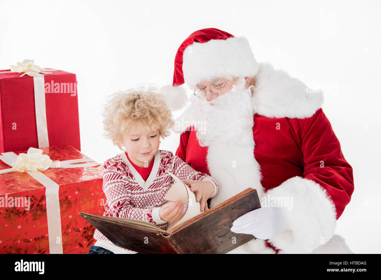 Santa Claus and kid sitting and reading a book together near gift boxes ...