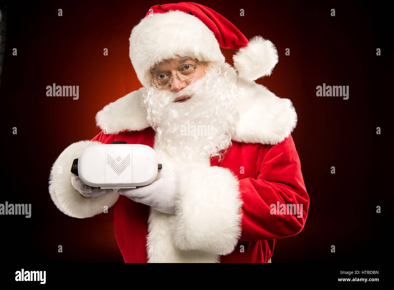 Santa Claus showing virtual reality headset on dark red background ...