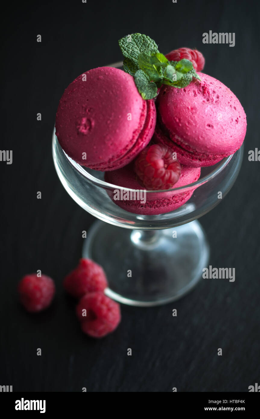 pink macaroons with raspberries in cup on black background Stock Photo ...