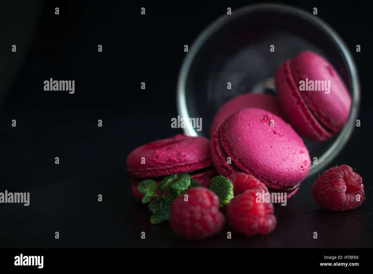 pink macaroons with raspberries in cup on black background Stock Photo ...