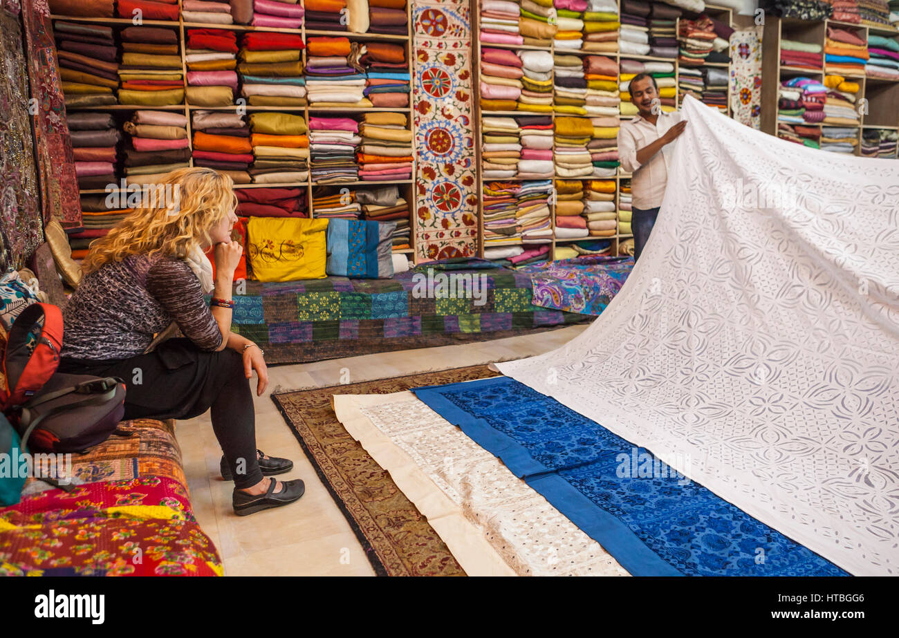 A woman sits and views textiles being shown by a salesman in a show ...