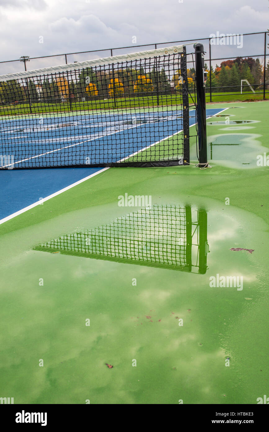 A tennis net is reflected in a pool of rain water on a blue and green ...