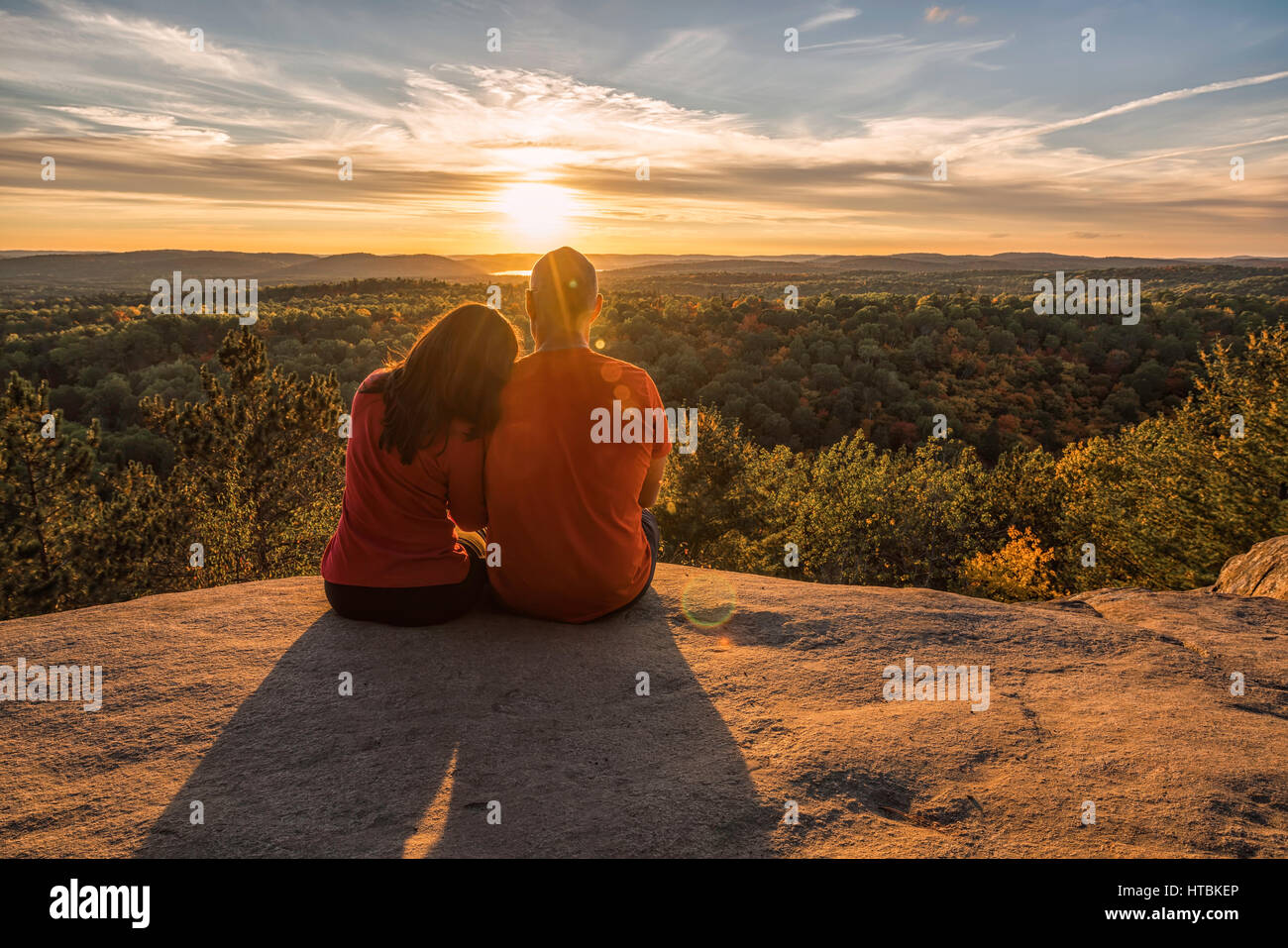 Couple sitting on a cliff overlooking Algonquin Park at sunset; Ontario ...