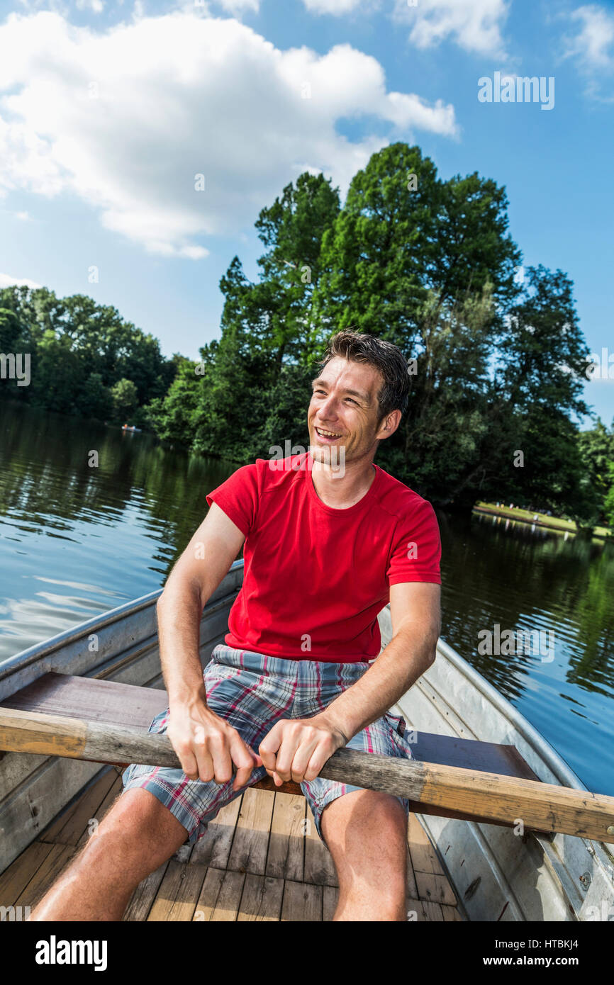 A smiling man rowing a boat down a calm river on a clear sunny day ...