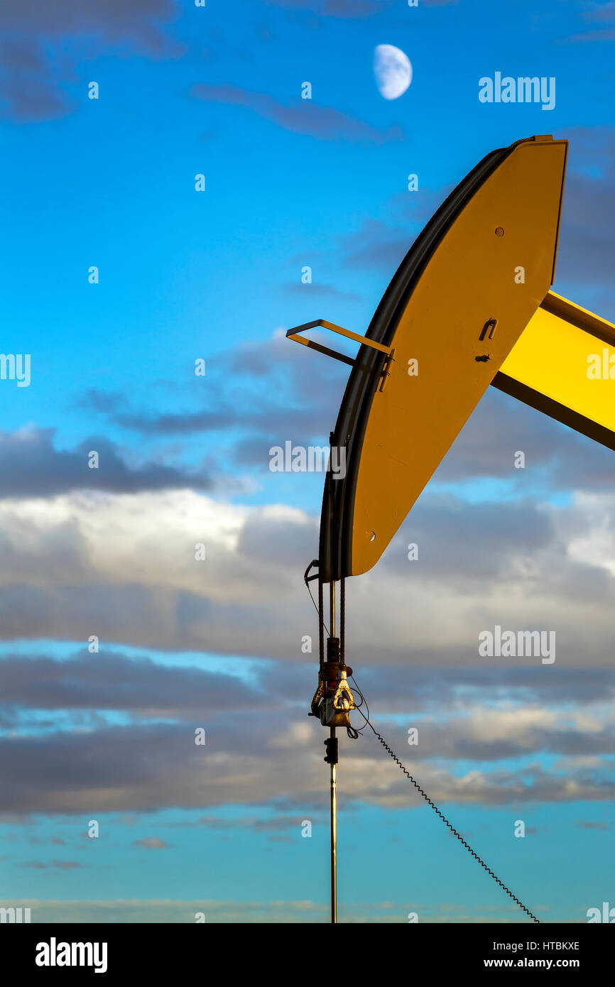 Close up of pump jack head with blue sky, clouds and moon in the sky ...