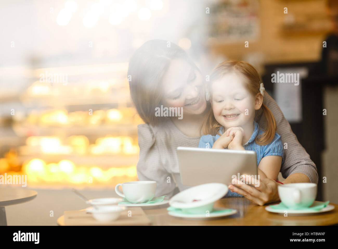 Woman showing her daughter interesting cartoon in touchpad while ...