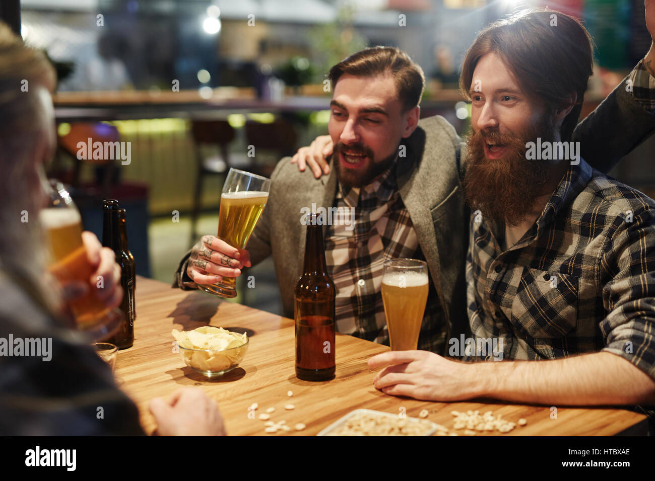 Drunk buddies cheering with beer and talking by table in pub Stock ...