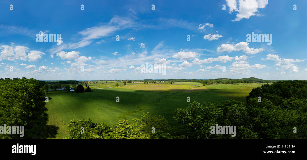 Blue Sky over a green field with spots of sunlight. Trees surround this ...