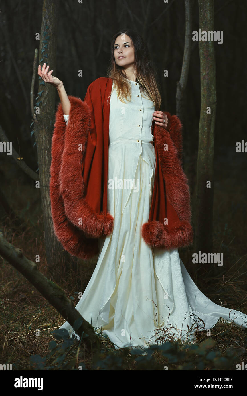 Beautiful young woman posing with elegant red cloak. Fantasy woods ...